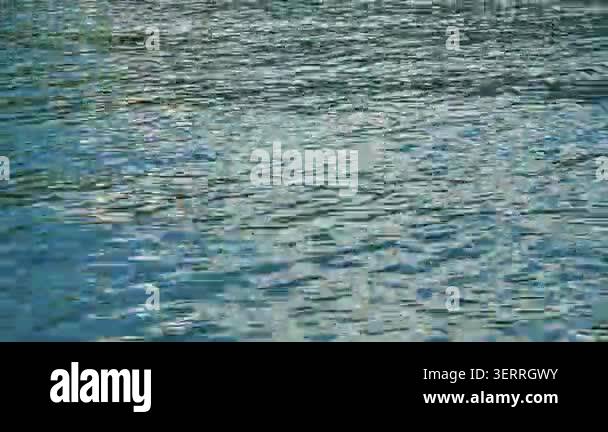 Water ripples move across a reflective surface in a static shot ...