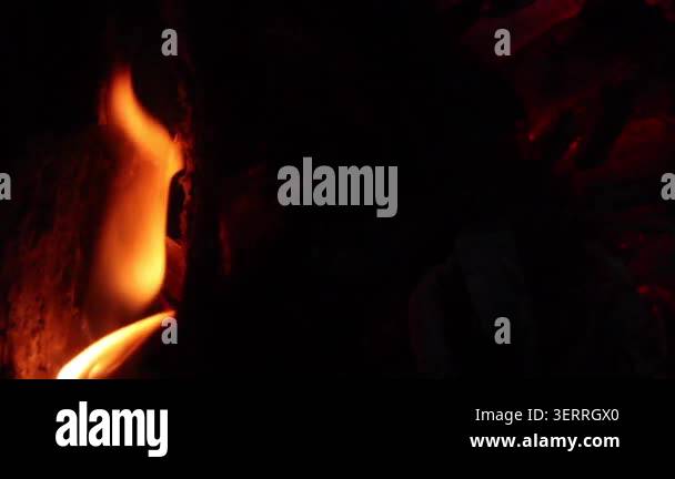 Close-up of a bright orange flame burning on wood in a dark environment ...