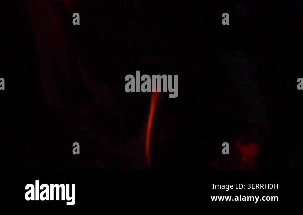 Close-up of a curved orange flame glowing against a dark background ...