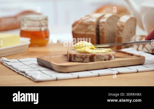 Soft butter spreading with a knife on a slice of fresh bread on wooden ...