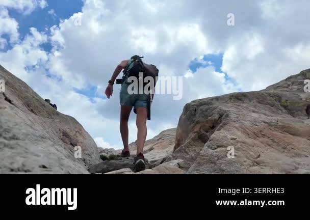 woman hiker with a backpack stands on a rocky peak, gazing at a vast ...