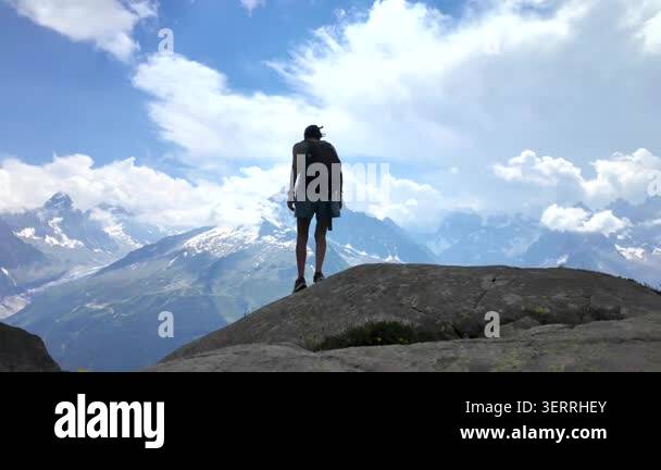 woman hiker with a backpack stands on a rocky peak, gazing at a vast ...