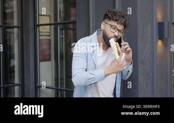 Busy young man eating and talking on the phone outdoors Stock Video ...