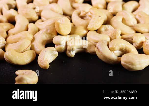 Cashew nuts falling from above onto a pile of cashews filled on a black ...