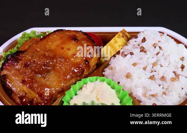 Rotating chicken teriyaki bento box on a black background, close up ...