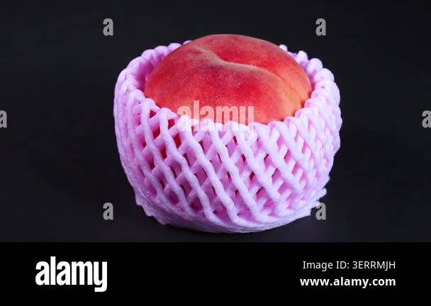 Close-up of a Single White Peach in a Foam Net Rotating Against a Black ...