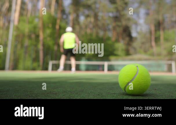 A tennis ball rests on the court while a person plays tennis in the ...