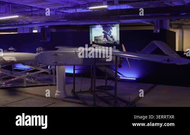 A drone is displayed indoors on a stand, with a screen showing footage ...