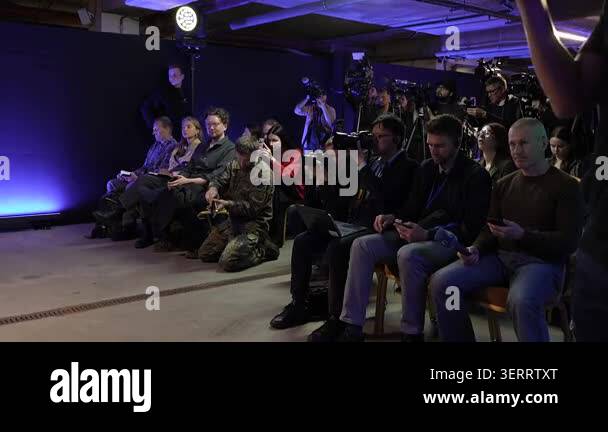 A group of people, including journalists with cameras, are seated and ...