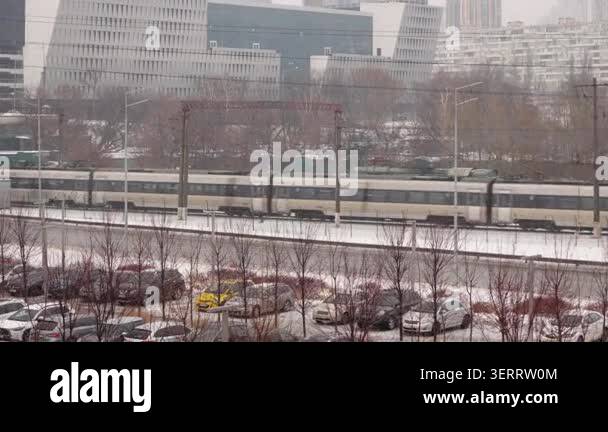 A modern high-speed train passes by a green locomotive on a snowy day ...