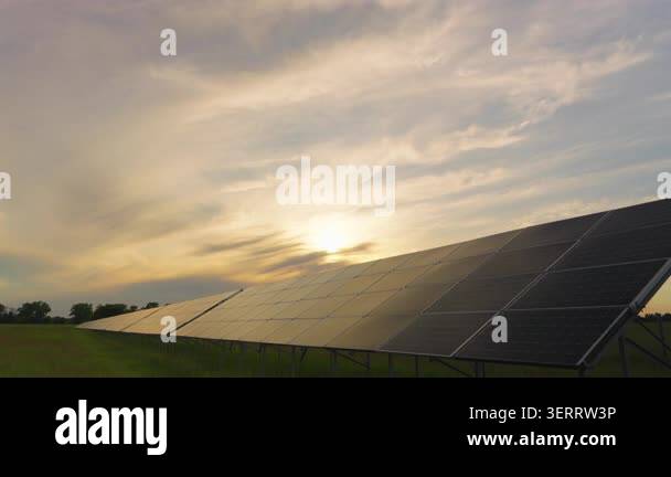 Solar panels in a field at sunset, with the sun peeking through the ...