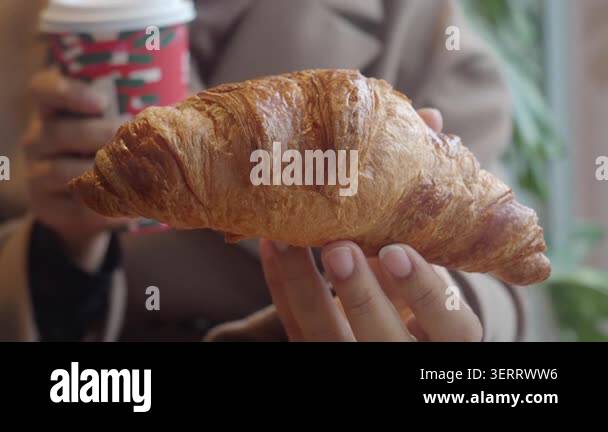 A person holds a croissant and a coffee cup in a cafe setting Stock ...