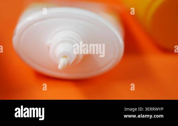 A close view of a white squeeze bottle cap placed on an orange surface ...