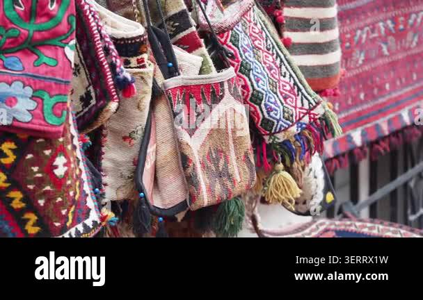 People walk by colorful bags and rugs hanging for sale in a market ...
