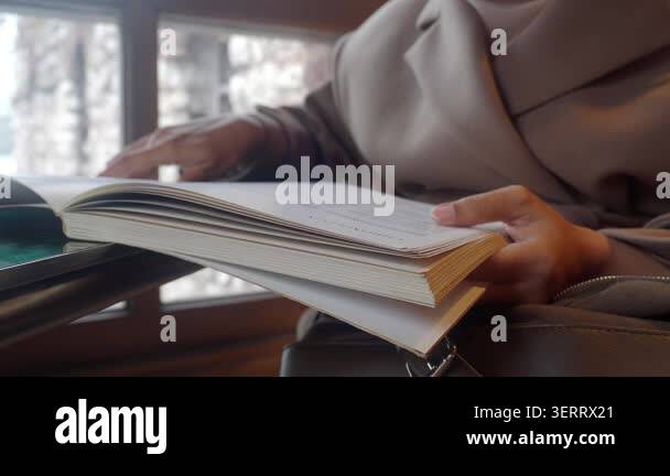 A person sits at a table and reads a book while looking out the window ...