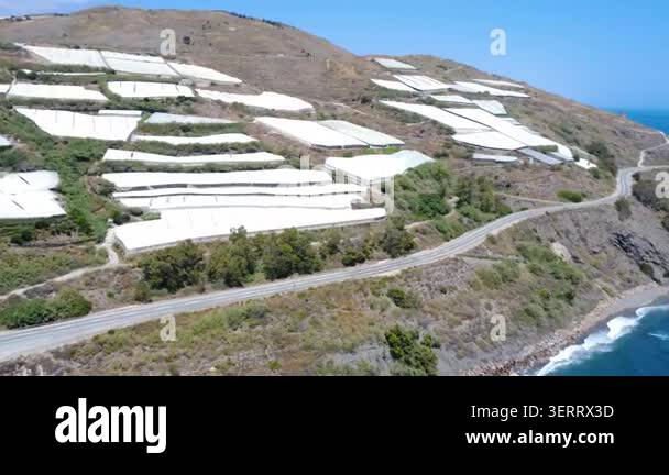Vast expanses of greenhouses lining the steep slopes of a coastal cliff ...