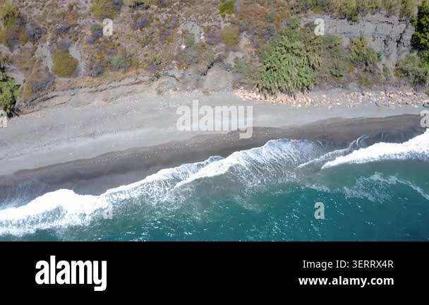 Drone view flying backwards from the turquoise sea over a pebble beach ...