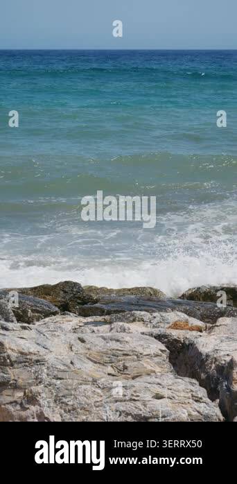 Ocean waves crashing white foam on a rocky beach shoreline under a blue ...
