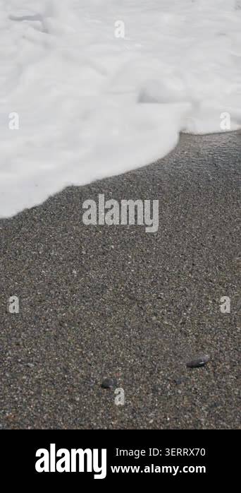 White ocean foam washing onto a dark pebble beach, creating a natural ...
