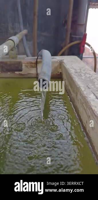 Clean water flowing from a metal pipe into a concrete basin, creating ...