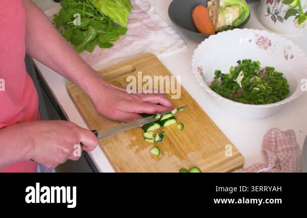In a kitchen, a woman is busy slicing cucumbers on a cutting board. She ...