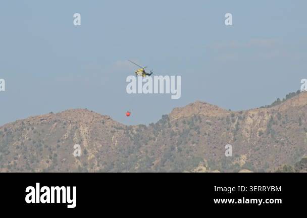 A helicopter hovers over rugged mountain terrain. The scene conveys the ...