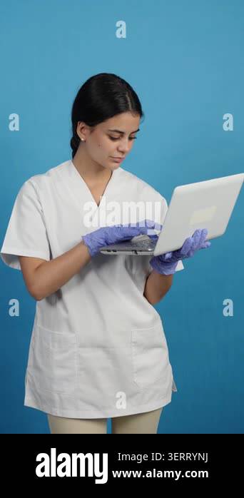 Young medical professional in a white uniform and gloves typing on a ...