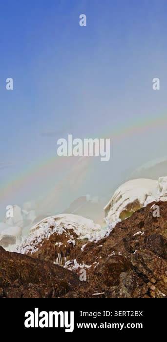 Ice covers the ground with rocky surfaces visible. A rainbow arcs ...
