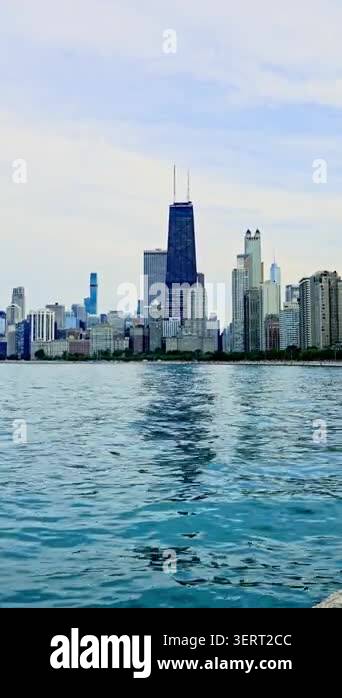 City buildings rise tall near a body of water under a light blue sky ...