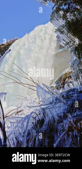 Water from a waterfall crashes down, surrounded by icicles and frosty ...