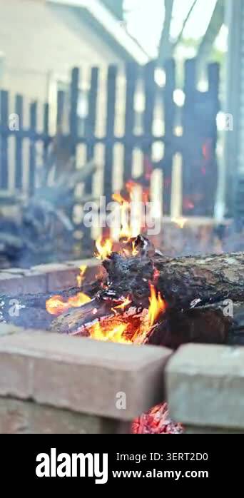 A fire burns in a fire pit as logs crackle and smoke rises into the air ...