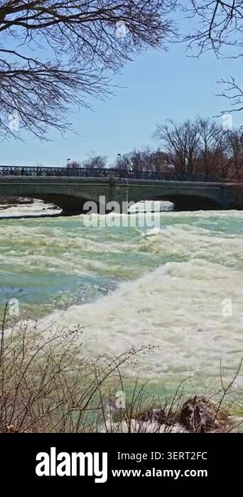 Water moves swiftly beneath a stone bridge as trees stand nearby and ...