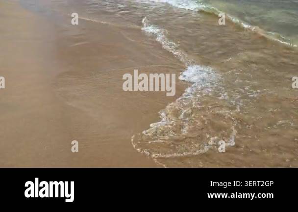 Waves roll over the sandy shore as the tide comes in at the beach. The ...