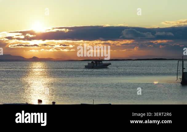 A solitary fishing boat sailing across the sea in golden sunset light ...