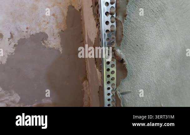 Close-up of a worker applying plaster over a metal corner bead profile ...