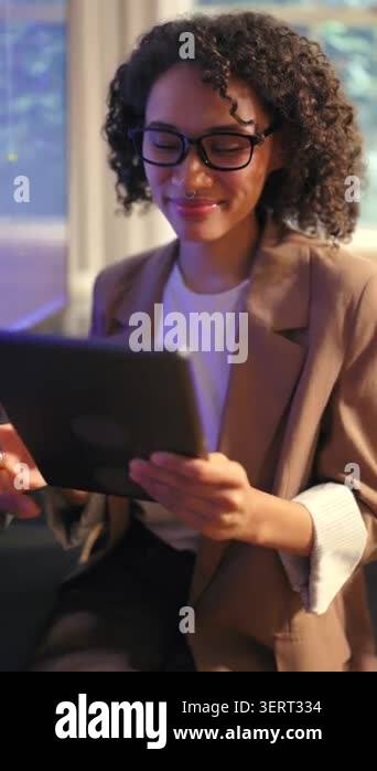 Smiling professional woman sits near a large window holding a tablet ...