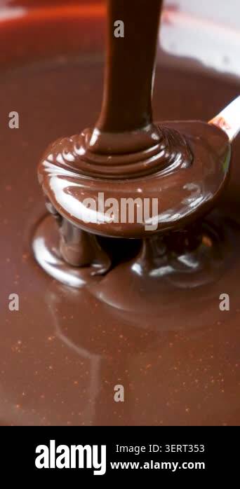 Macro shot of thick glossy chocolate sauce pouring and creating swirls ...