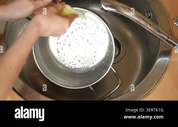 Hands washing and rinsing dirty stainless steel pot under kitchen ...