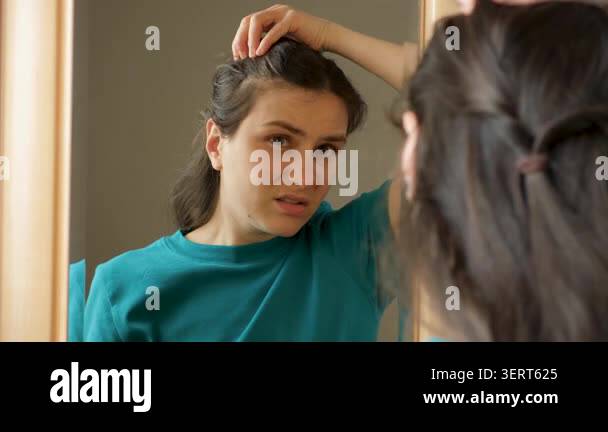 Concerned female looking at her reflection and observing thinning hair ...