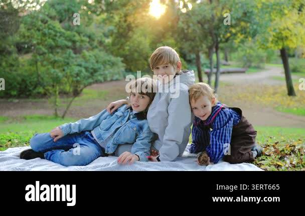 Three smiling children sit close together on a white blanket in a ...