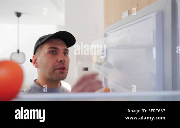 Young man in black baseball cap peers into open refrigerator searching ...