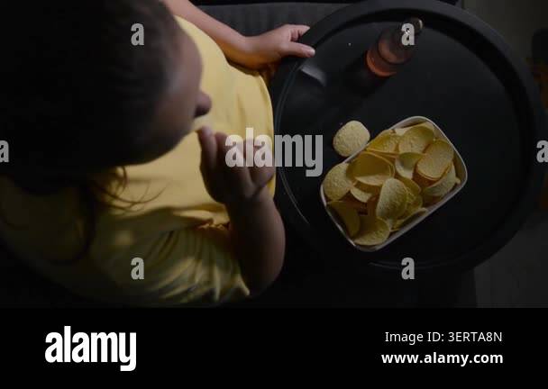 Top view of a young woman eating potato chips while watching a movie ...
