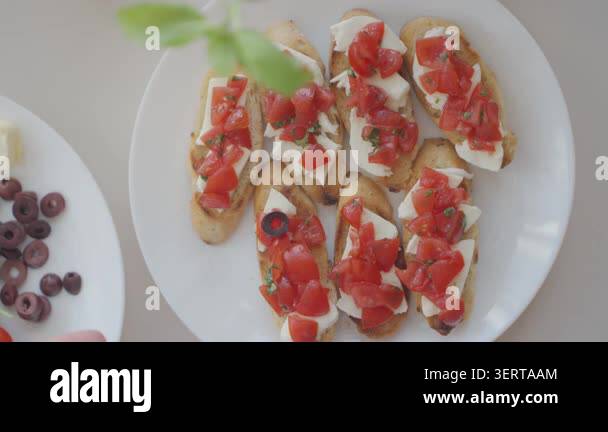 Hand adds black olive slices to bruschetta with tomato and mozzarella ...