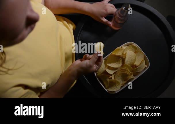 Top view of a young woman eating potato chips while watching a movie ...