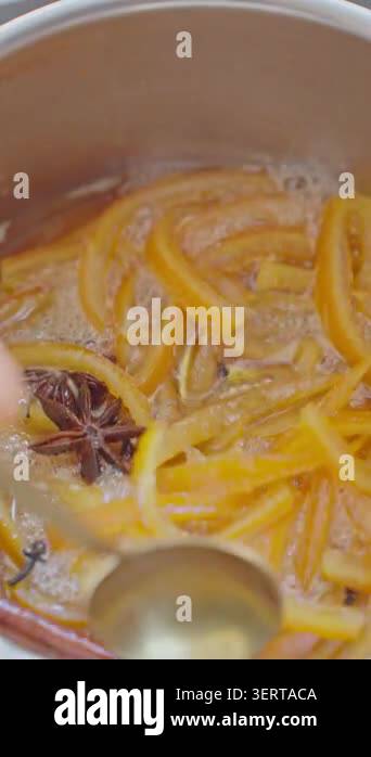 Spoon stirs candied orange peel in bubbling syrup with star anise ...