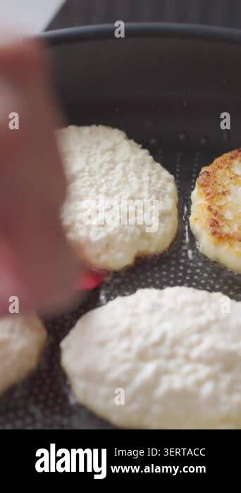 Cottage cheese pancake is turned with spatula in frying pan as another ...