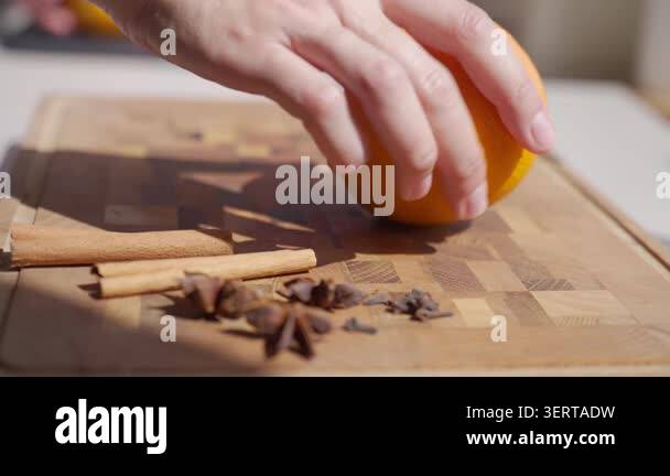 Hand places oranges on cutting board beside cinnamon sticks, star anise ...