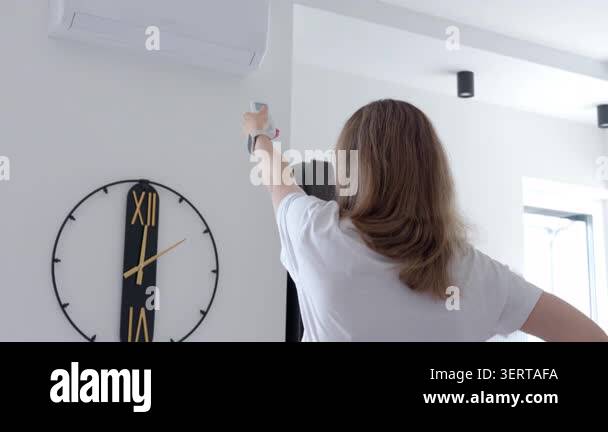 Woman uses a remote control to turn on a wall air conditioner at home ...