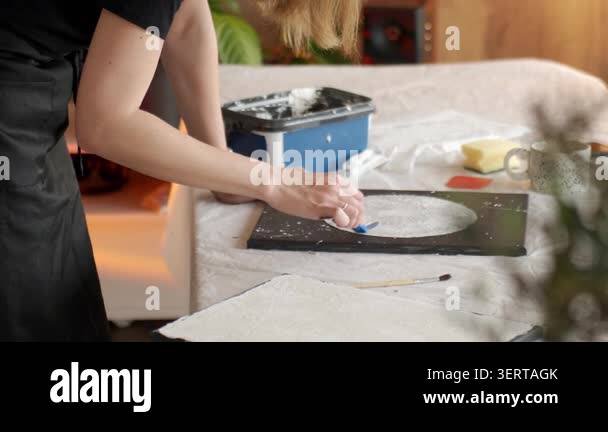 Woman spreads white plaster paste on black canvas with palette knife at ...