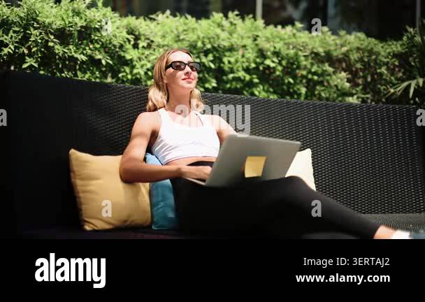 A woman wearing sunglasses is relaxing on a couch outdoors, holding a ...
